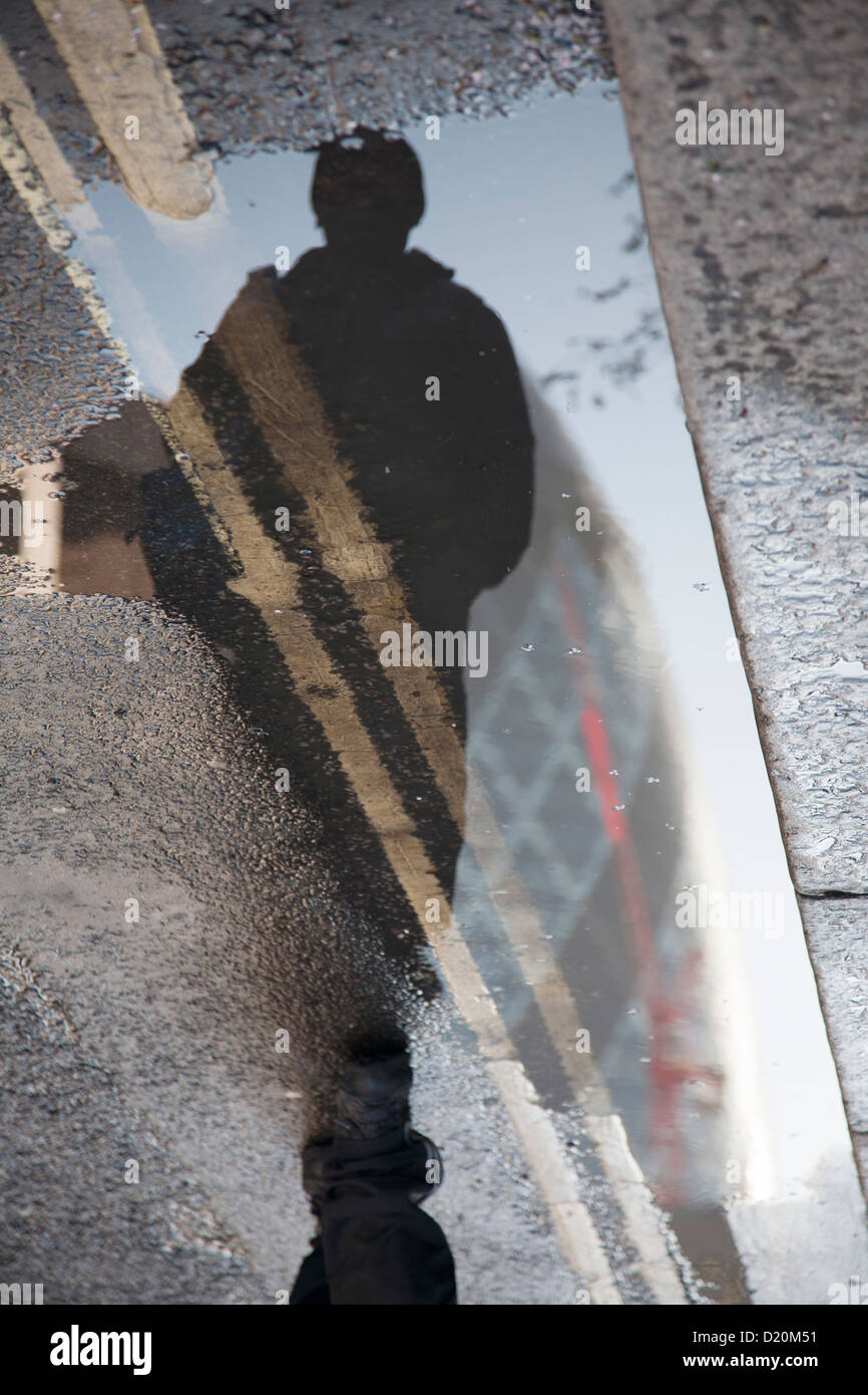 REflection of Gherkin and man in puddle by the roadside with yellow ...