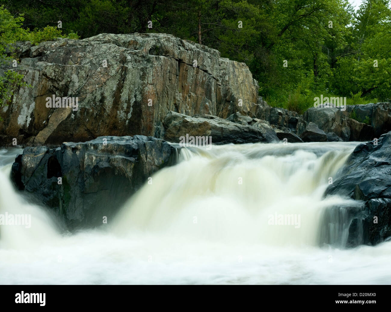water falling over rocks with blur movement against green trees ...