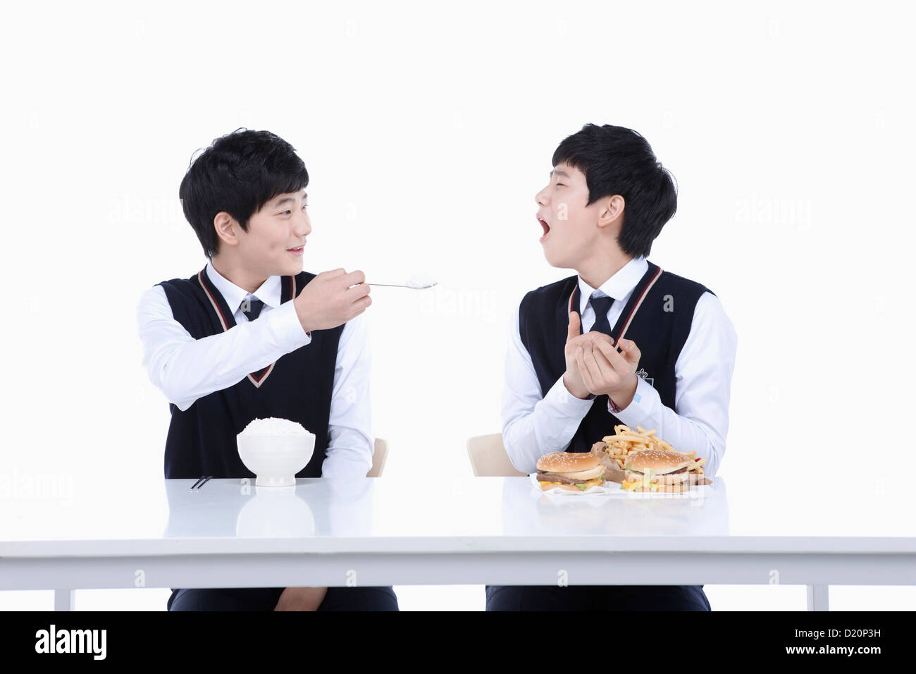 male student giving the other identical male student a spoon of rice ...