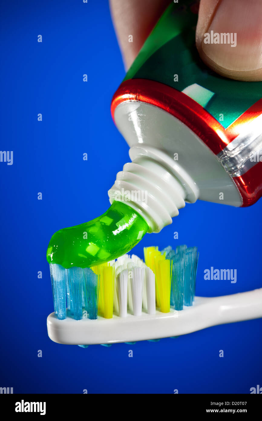 toothpaste being squeezed onto a toothbrush on a dark blue background ...