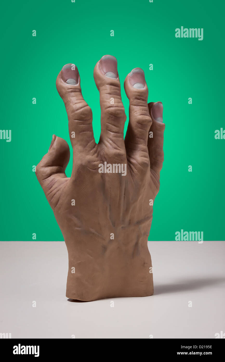 Huge fake hand standing on a white surface against green background ...