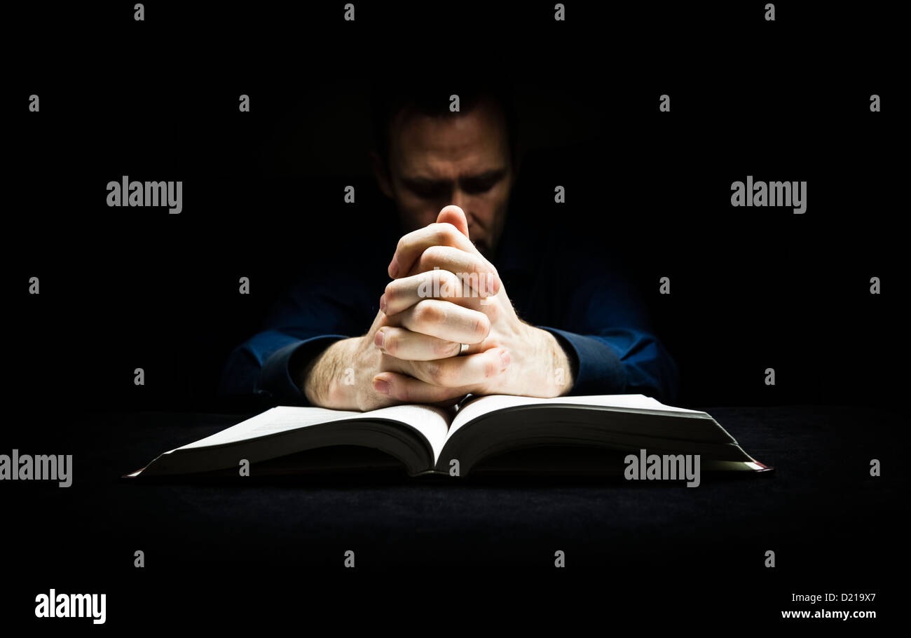 Man praying to God with his hands resting on a bible Stock Photo - Alamy