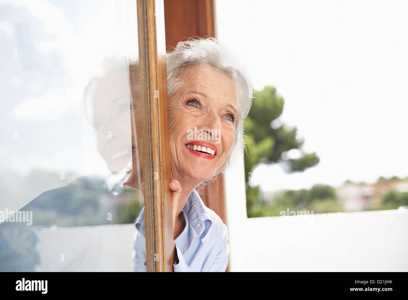 Spain, Senior woman looking through window, smiling Stock Photo - Alamy