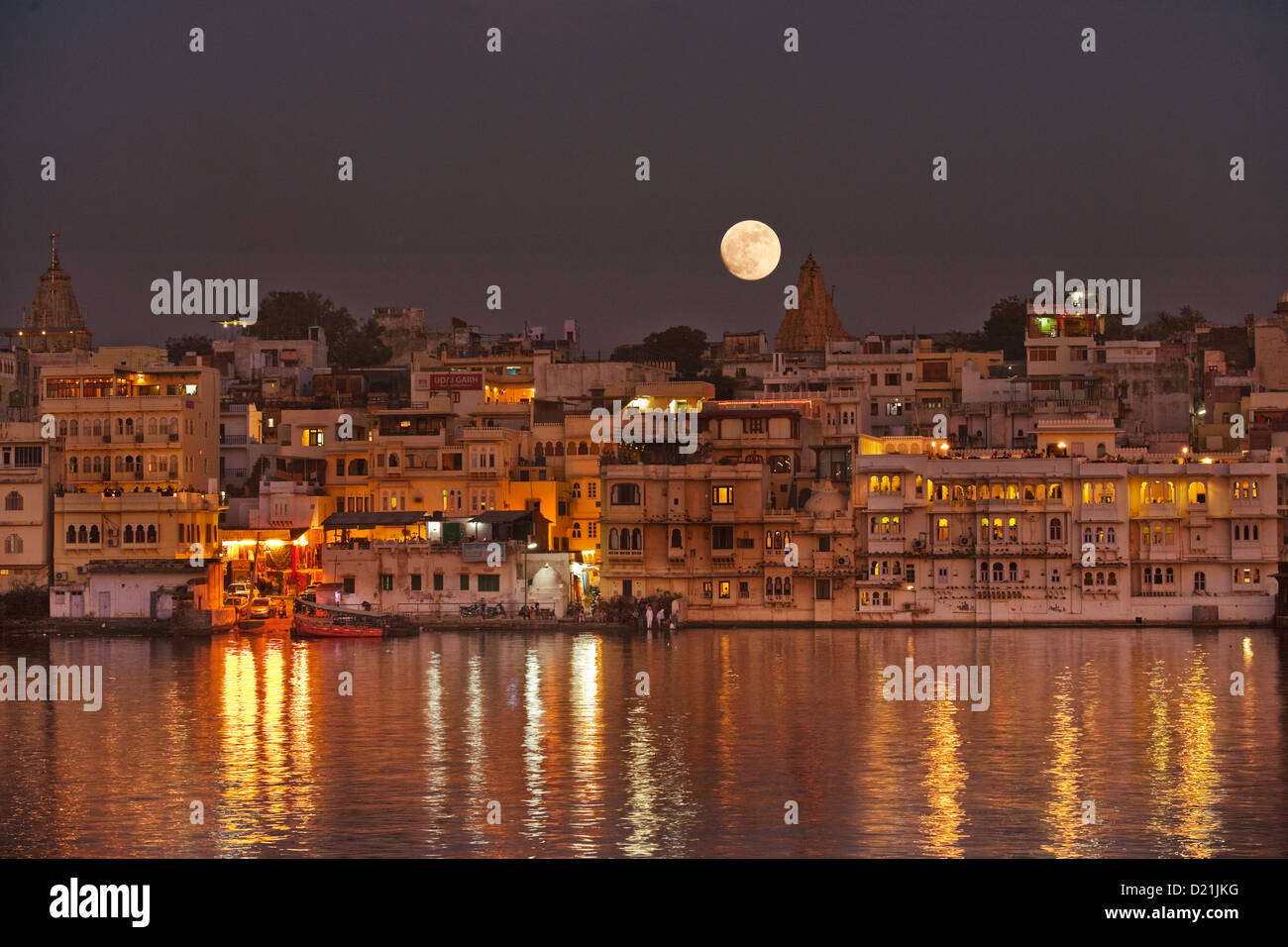 A full moon rises on a clear night over the city and temples of Udaipur ...