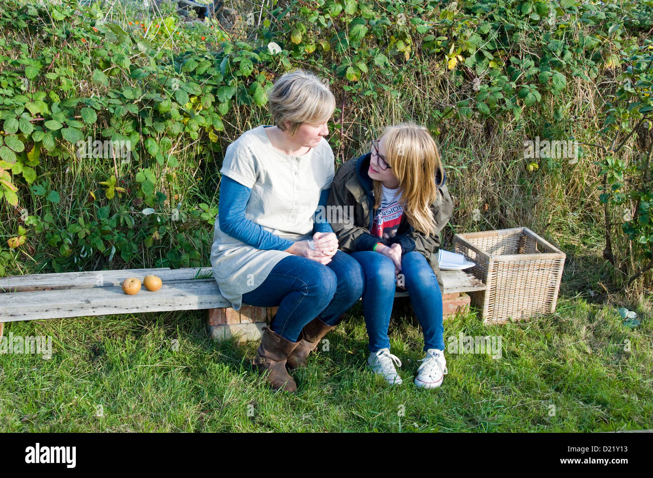 Mother and daughter on their allotment sitting on rustic bench made of ...