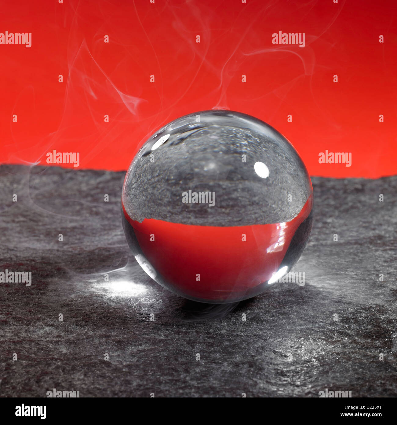 a clear crystal ball on rough dark grey stone surface in front of red ...