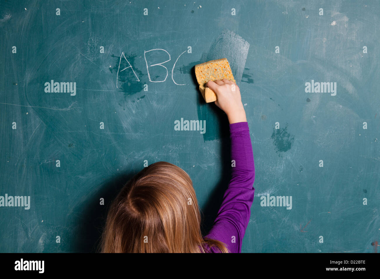 Young girl wiping letters written in chalk from chalkboard with wet ...