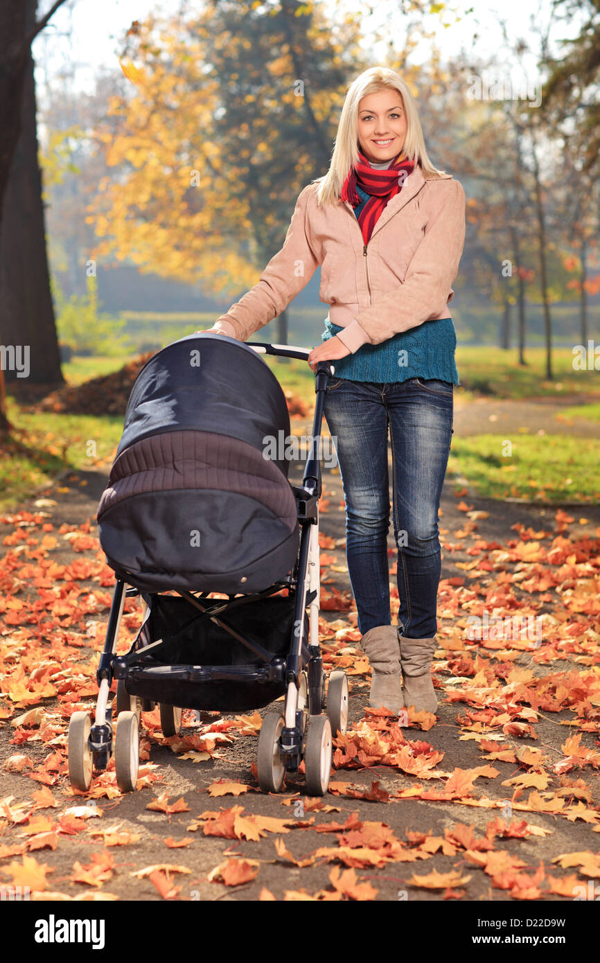 Young mother taking a walk in the park with her baby in a pushchair ...