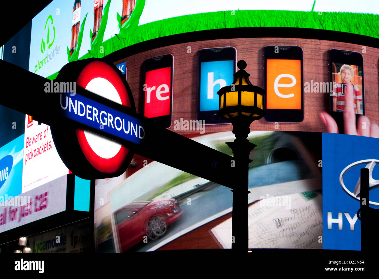 London Underground roundel at night with advertising LED screens behind ...