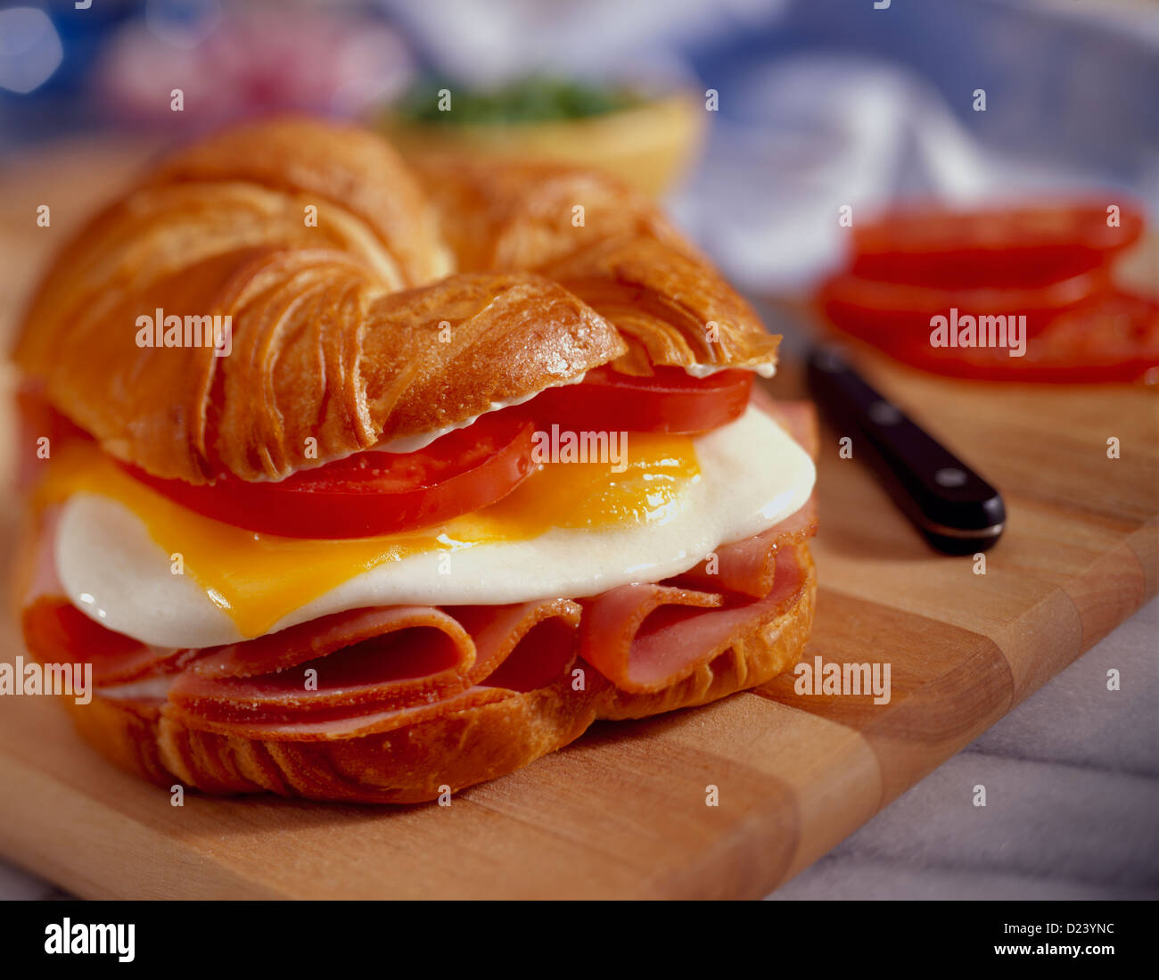 A breakfast croissant sandwich with ham, eggs, tomato and melted cheese ...