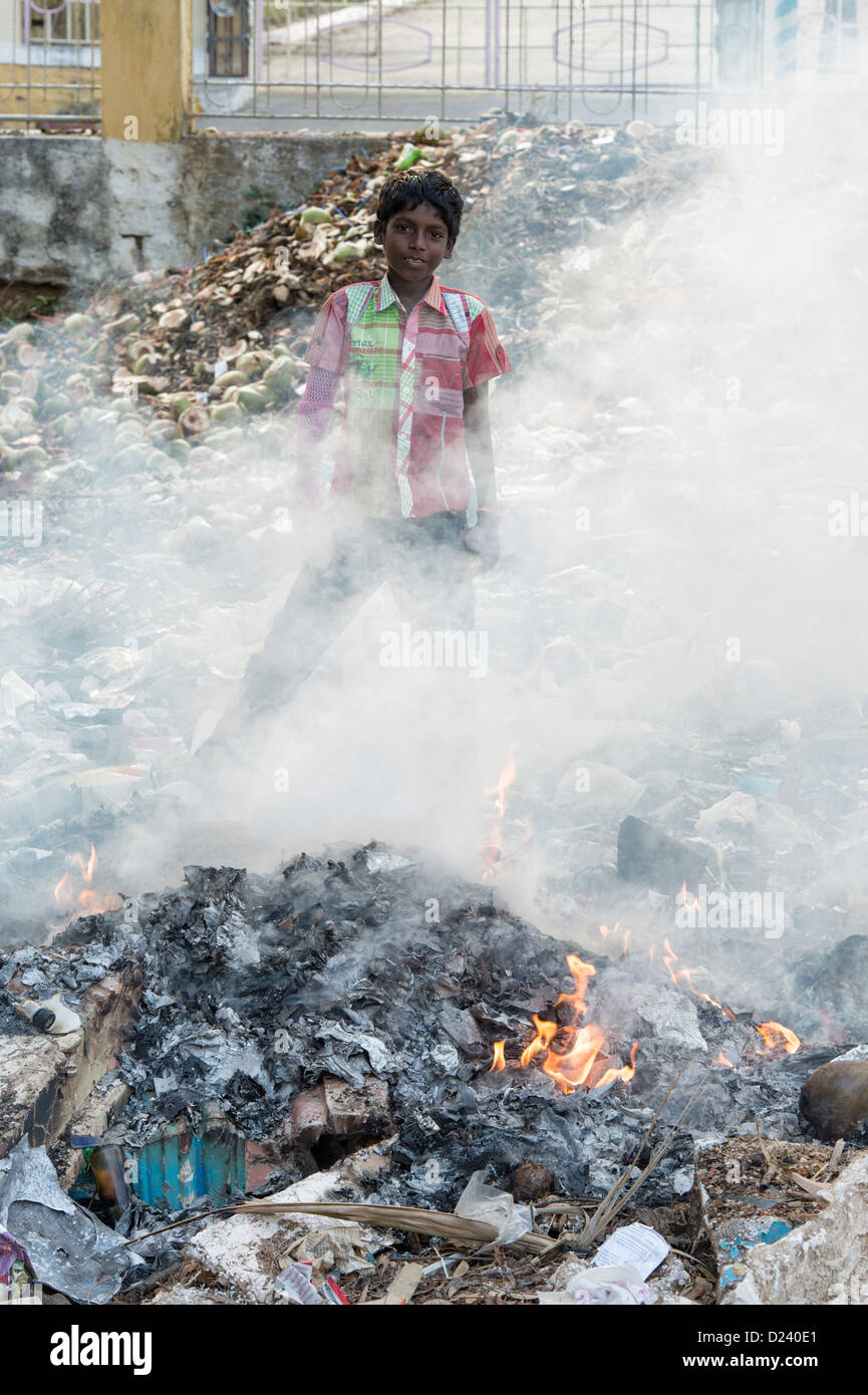 Indian boy standing in amongst burning household waste. Andhra Pradesh ...