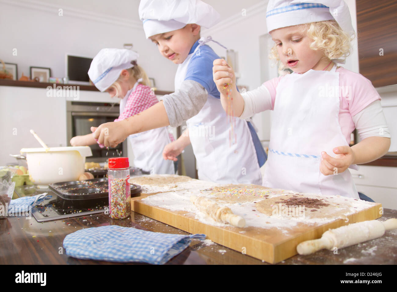 Germany, Girls and boy baking cup cakes and pouring sugar sprinkles ...