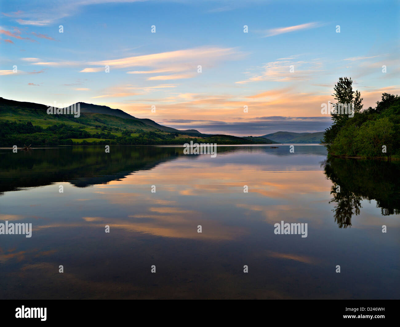 Sunset sky with distant hills and headlands reflected in calm water ...