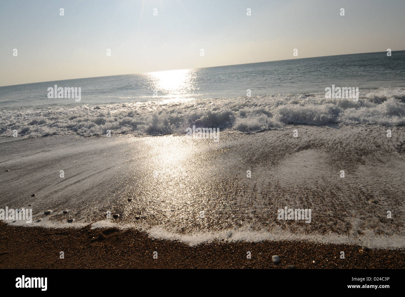 Waves lapping on beach with sun on the sea Stock Photo - Alamy