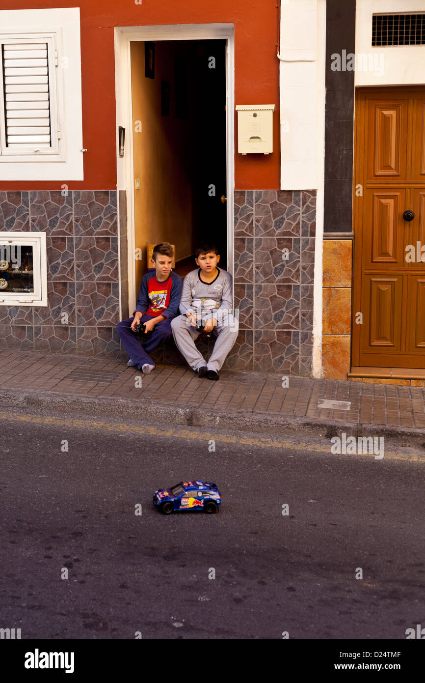 Two young boys sit on a front doorstep and play with remote control ...