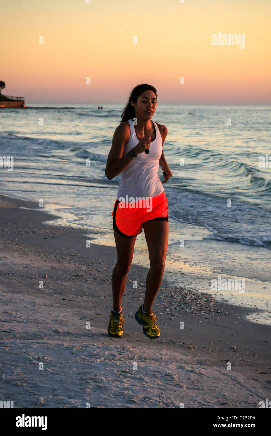 Young woman running along the Siesta Key beach in Florida at sunset ...
