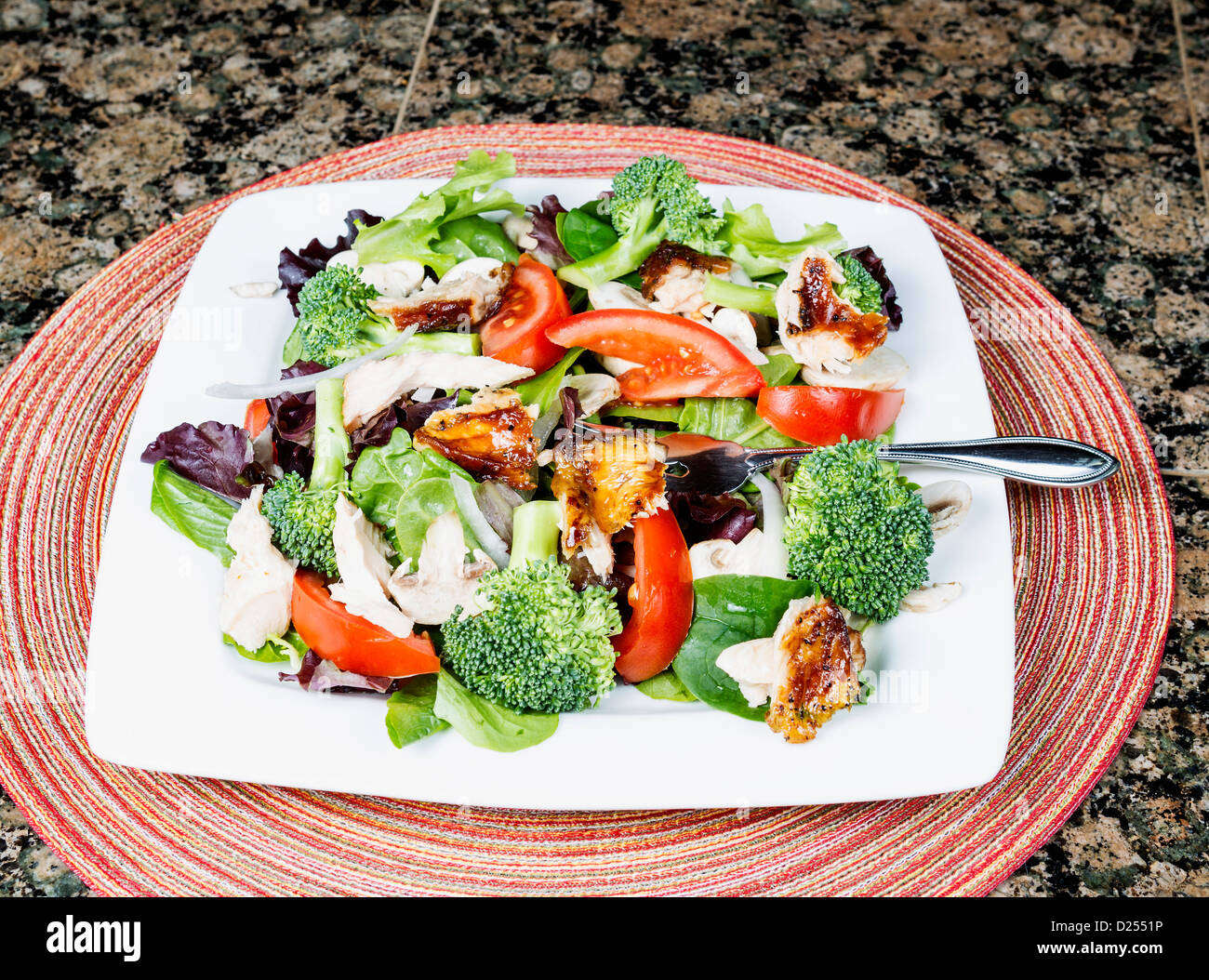 Fresh salad on white plate with fork and stone counter top in ...