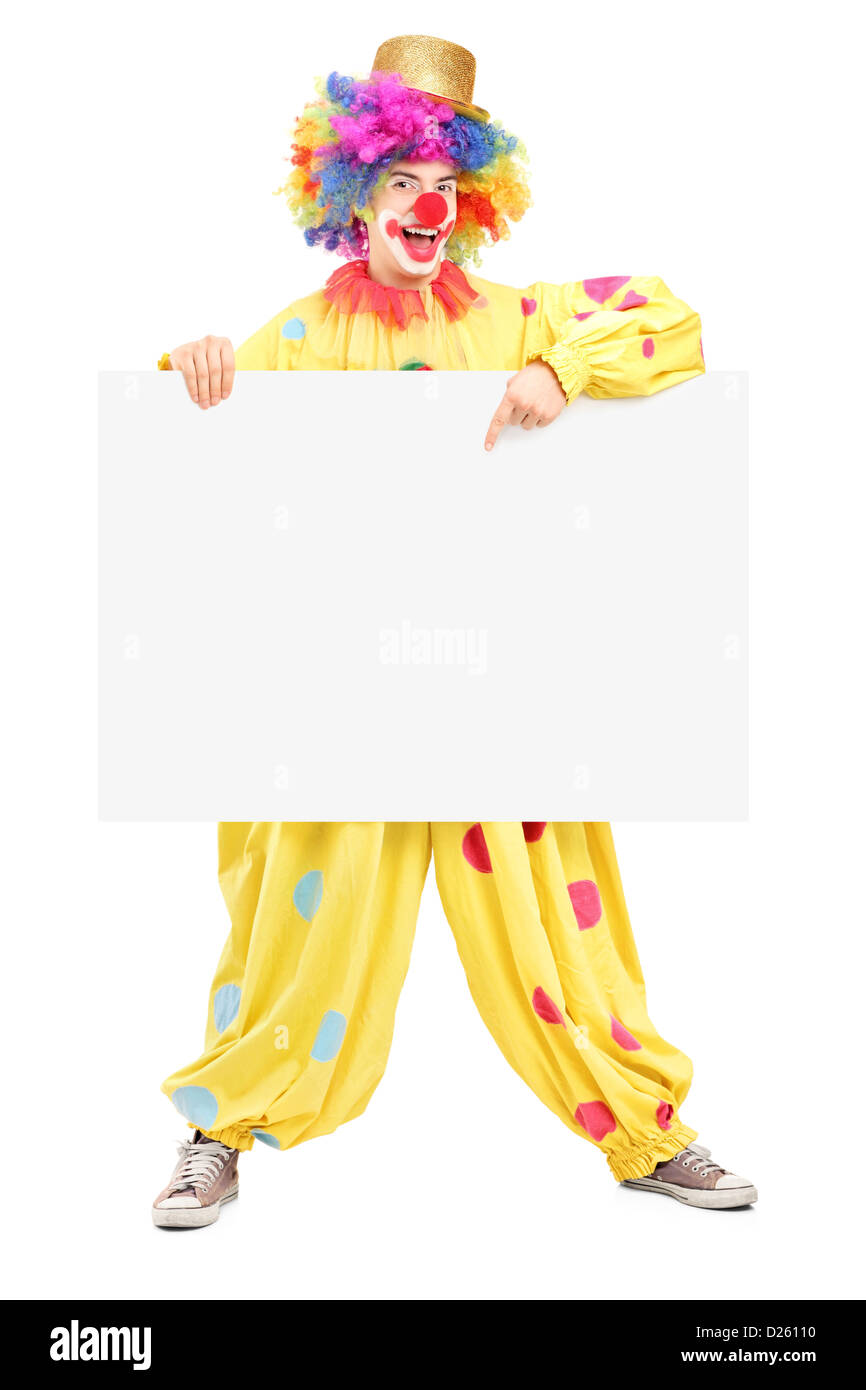 Full length portrait of a happy male clown pointing on a blank panel ...
