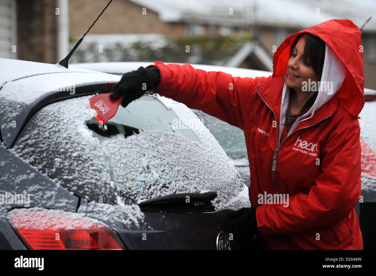 Young woman dressed in Heart FM radio station jacket clearing snow and ...