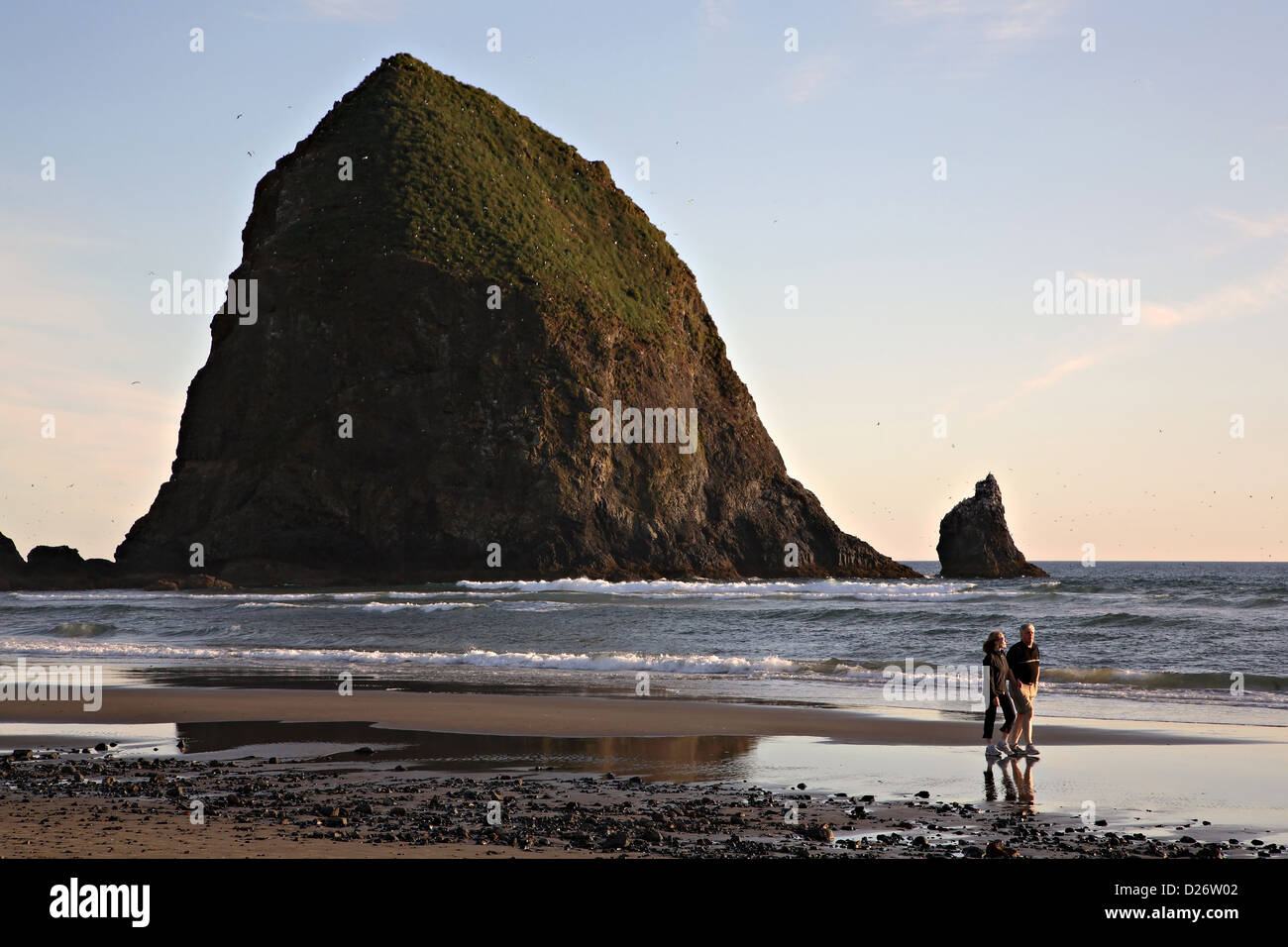 A couple walks along Cannon Beach near Haystack Rock in Oregon, USA ...