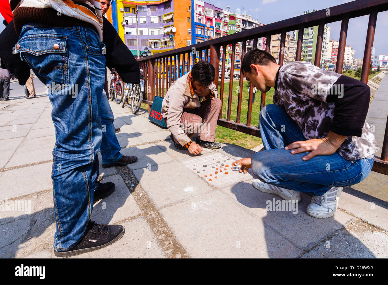 Young men playing checkers on the floor at a bridge over the Lana river ...