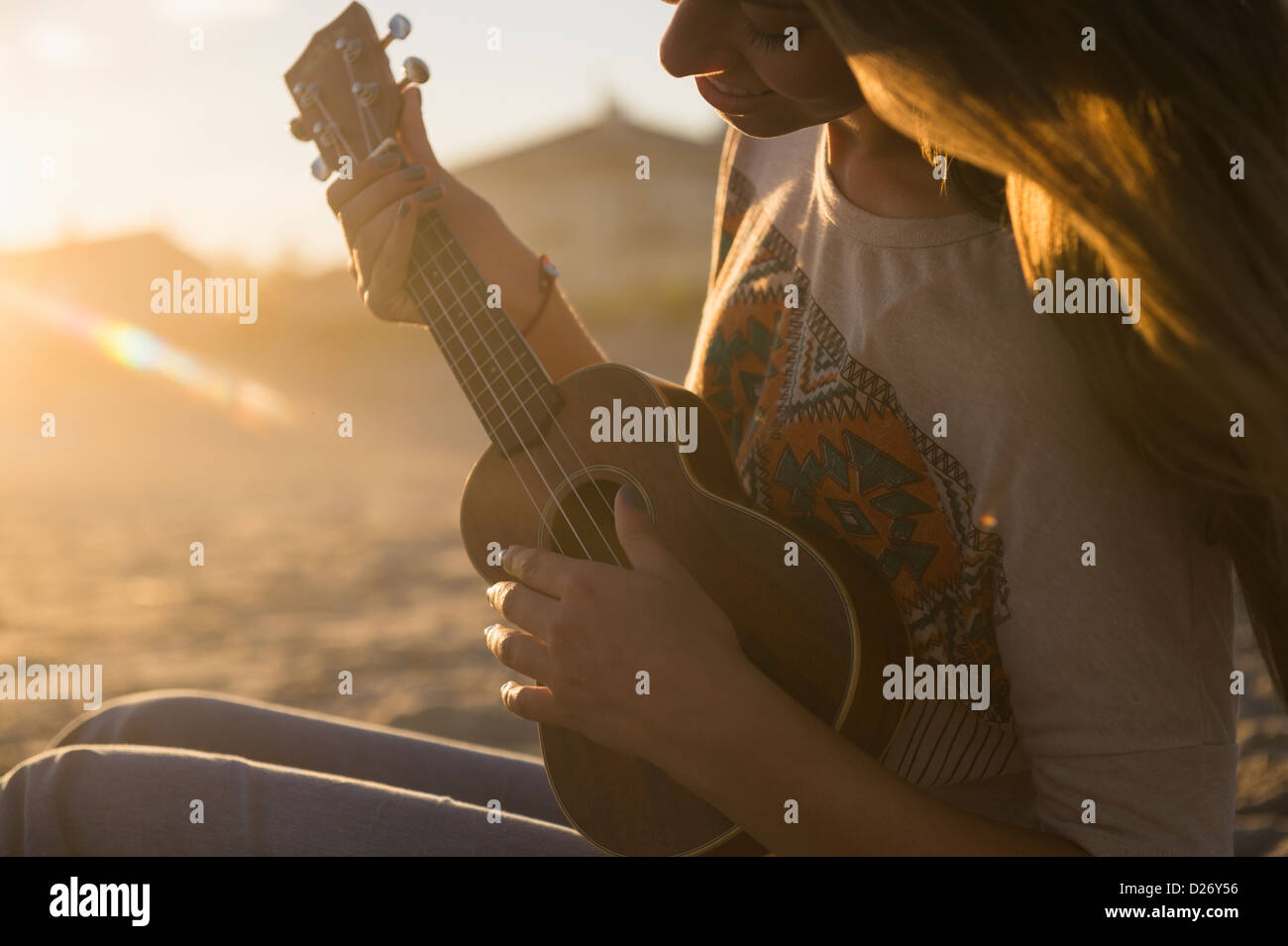 USA, New York State, Rockaway Beach, Woman playing ukulele at sunset ...