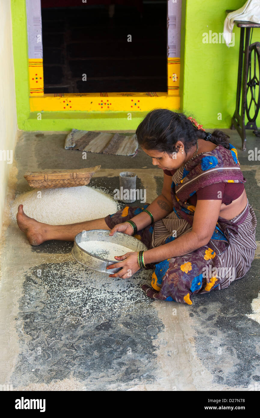 india woman sifting and cleaning rice outside her home in a rural ...