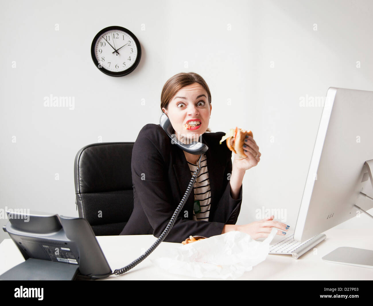Studio shot of young woman working in office and having lunch same time ...