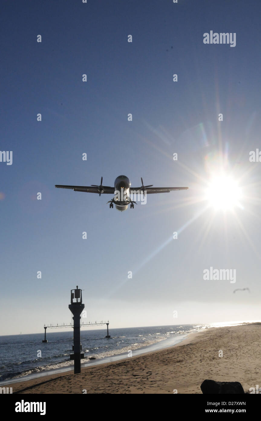 Propeller aircraft coming into land over beach with sun and blue sky in ...