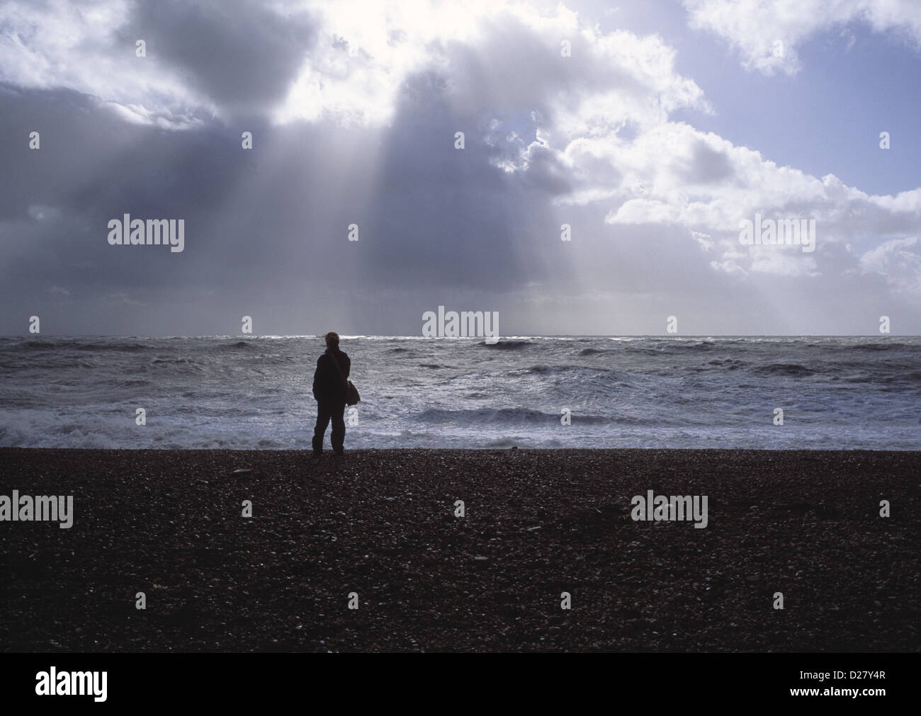 Silhouetted figure on beach, sunrays,clouds Stock Photo - Alamy