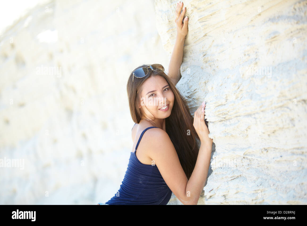 Cute brunette leaning against limestone wall and looking at camera ...