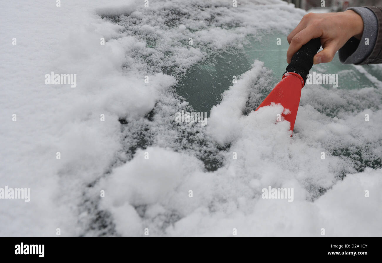 A young woman scratches snow and ice from the windscreen of her car in ...