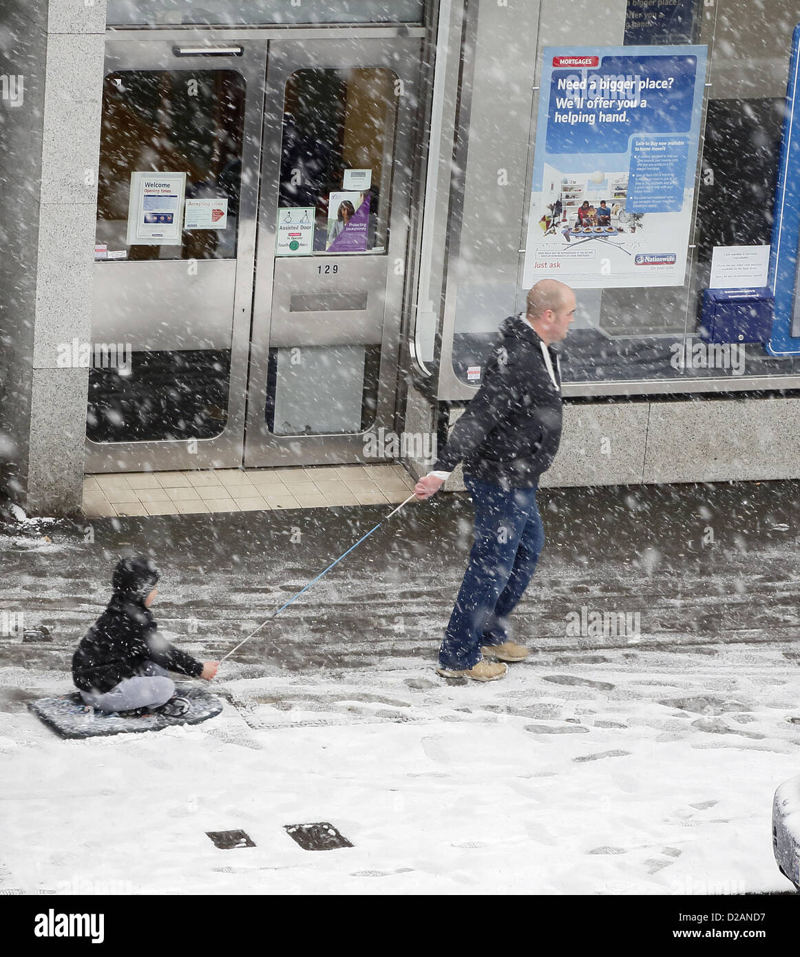 Man pulling a child on a sledge in the snow on a main road. Worcester ...
