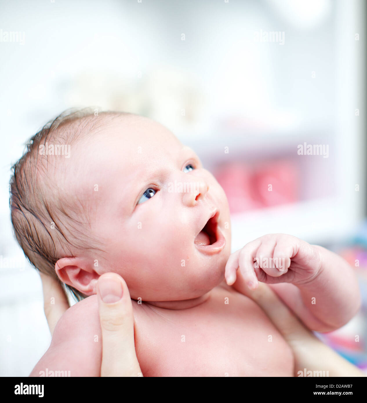 Adorable beautiful newborn baby cradled in its mothers hands looking up ...
