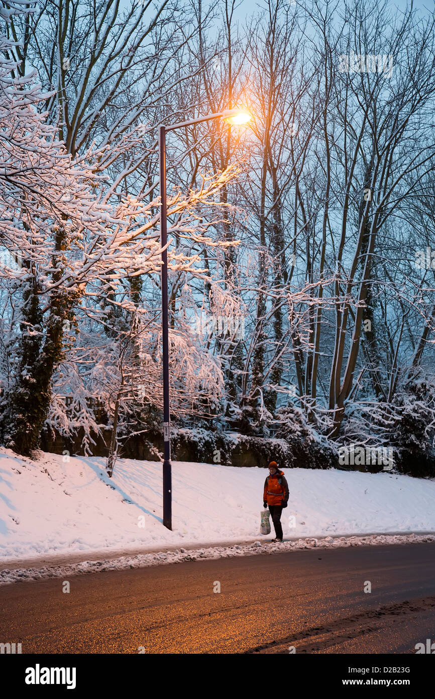 Woman walking with shopping bag in snow under street light, Abergavenny ...