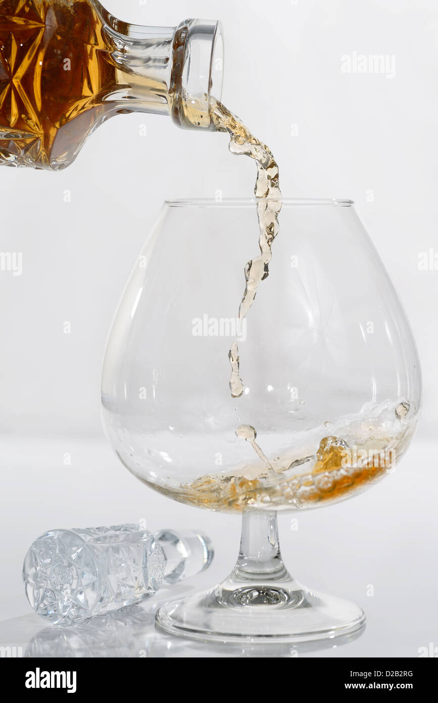 High speed frozen drops of pouring brandy from a crystal decanter into ...