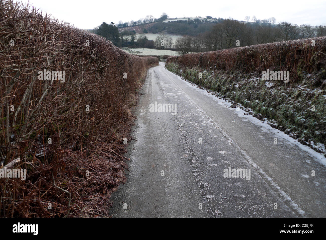 Black ice surface on a rural country lane lined with bare hedges during ...