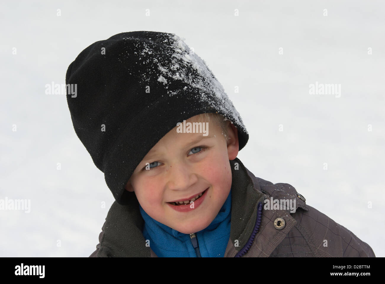 Boy (6-8) wearing black hat, winter, snow background, smiling, portrait ...