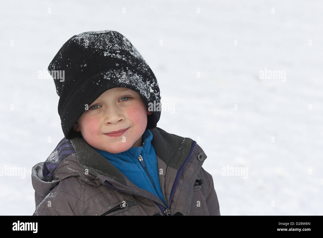 Boy (6-8) wearing black hat, winter, snow background, smiling, portrait ...