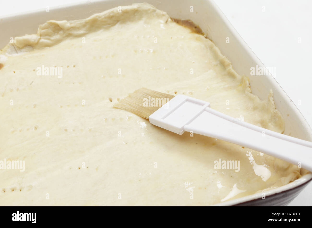 coating the surface of a meat pie with an egg and water mixture to ...