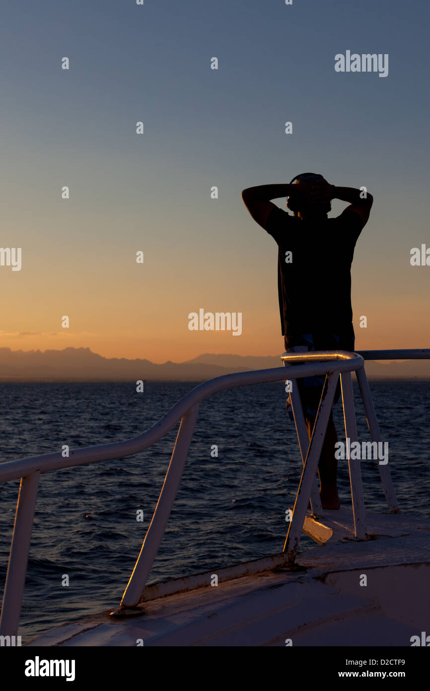 Person enjoying an ocean sunset standing on the prow of a ship looking ...