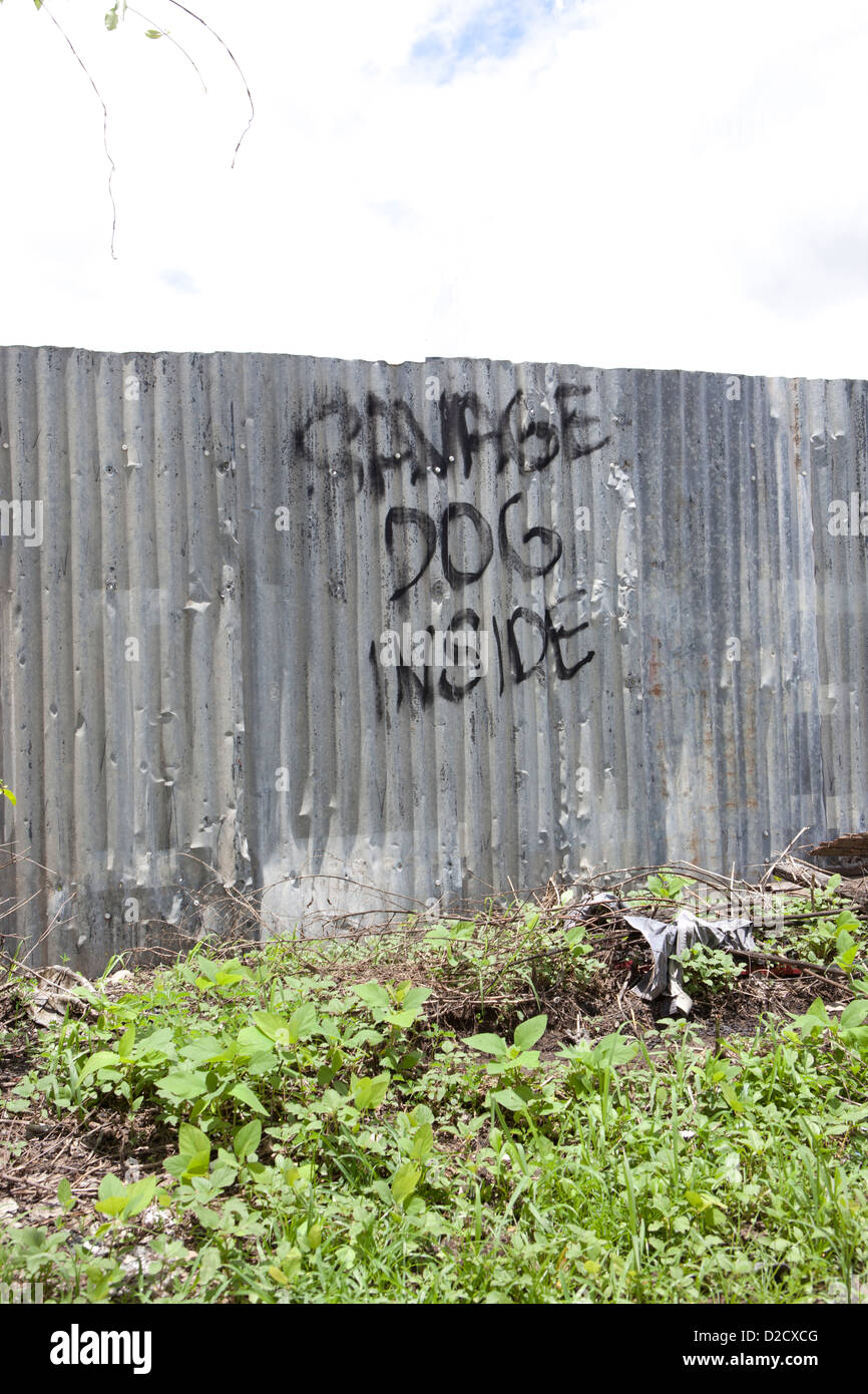 A handwritten warning sign on a tin fence saying 'Savage dog inside ...