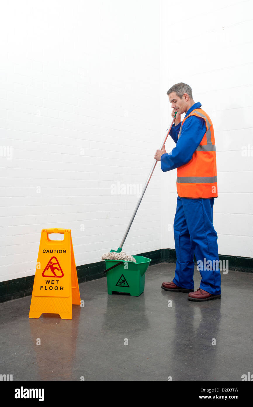 MODEL RELEASED Mopping floor Man mopping a floor next to a caution sign ...