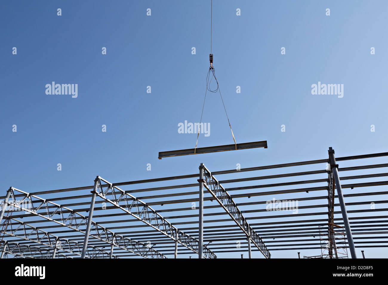 Crane lowering steel beam towards construction frame Stock Photo - Alamy