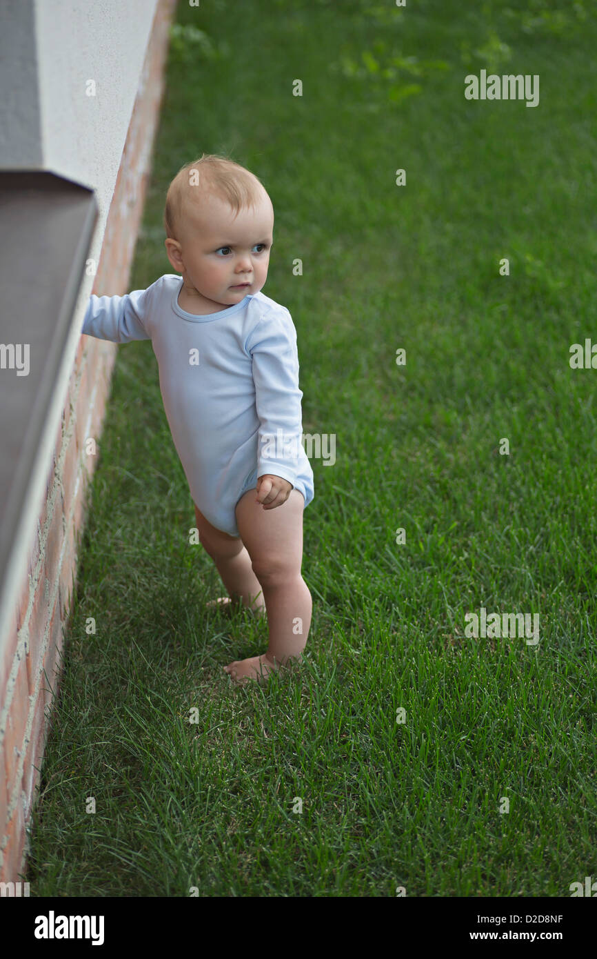 Baby in garden leaning against wall Stock Photo - Alamy