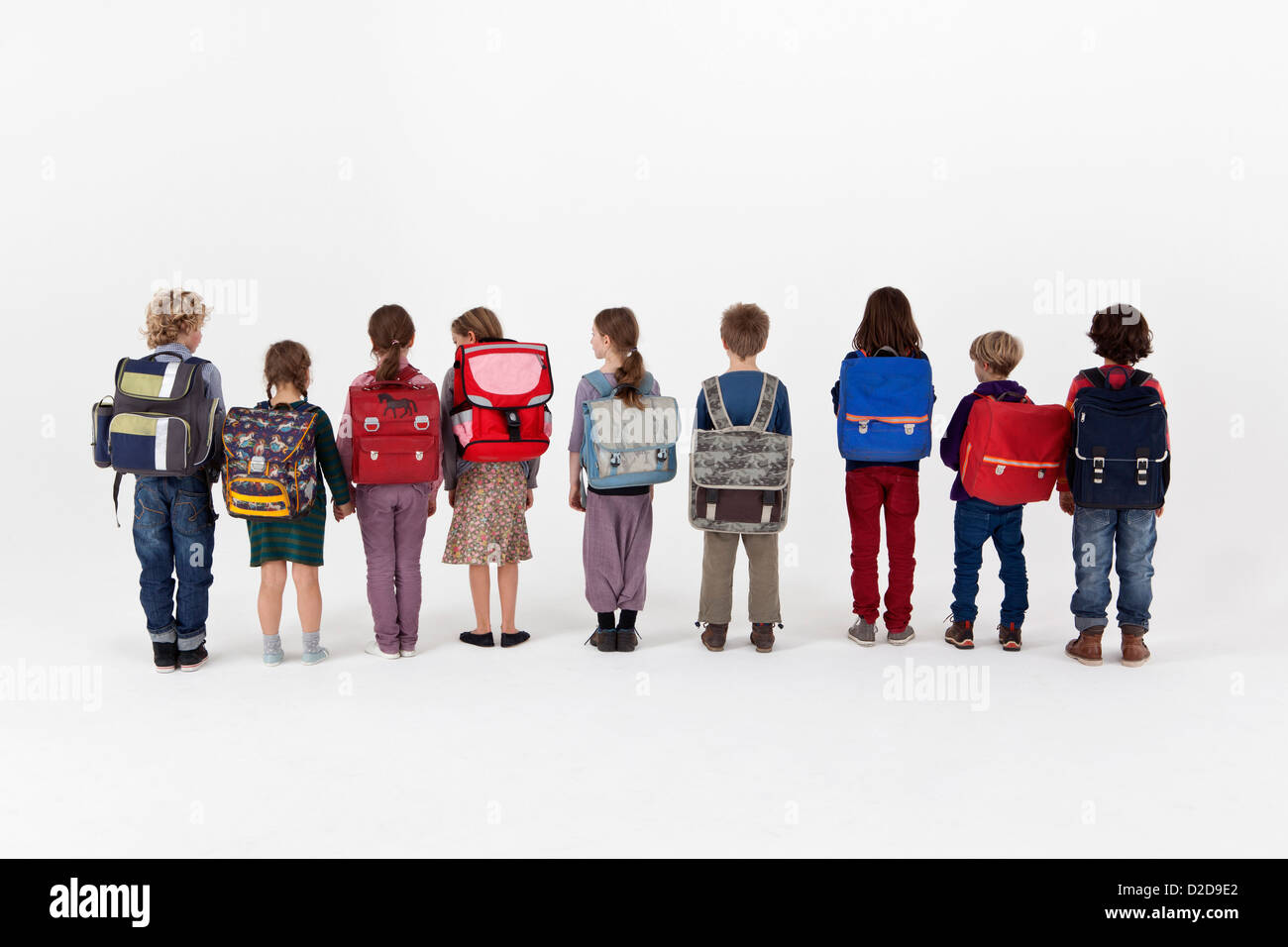 A group of school children wearing backpacks and standing in a row ...