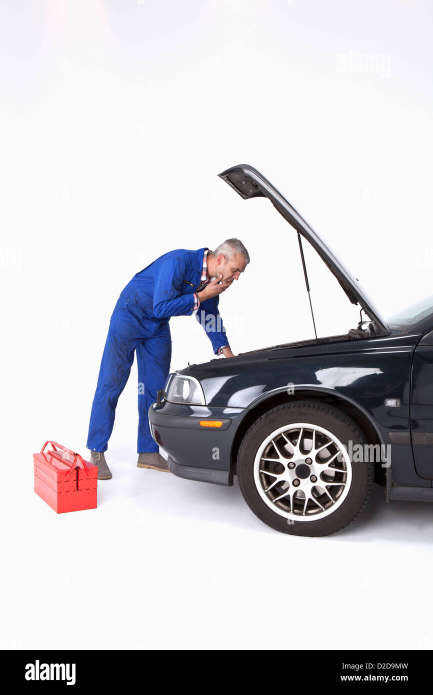 An auto mechanic looking under the hood of a car with uncertainty Stock ...