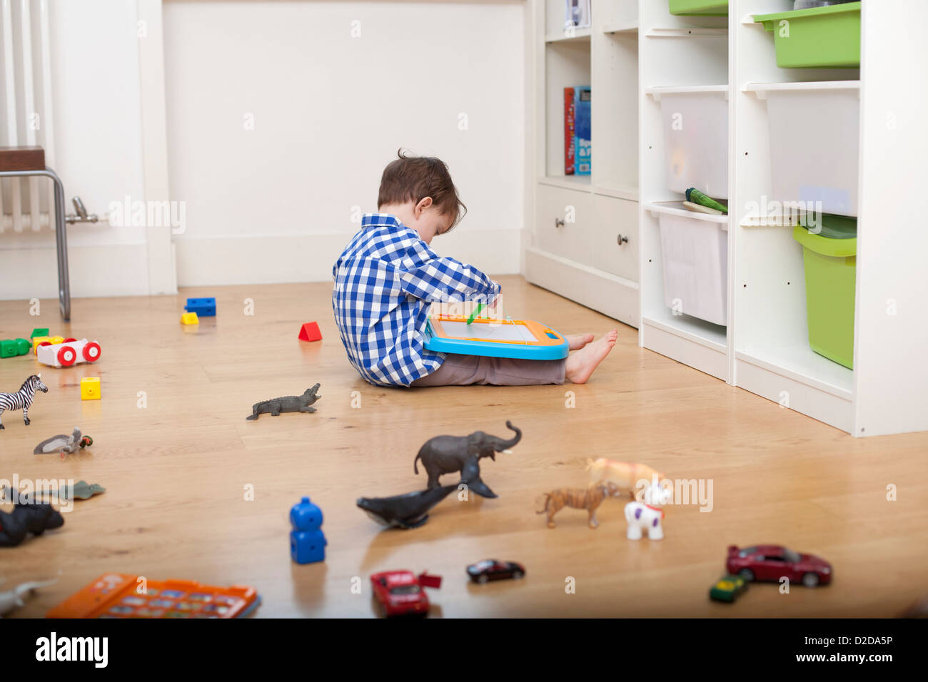 A boy sitting on the floor, drawing on a tablet, surrounded by various ...