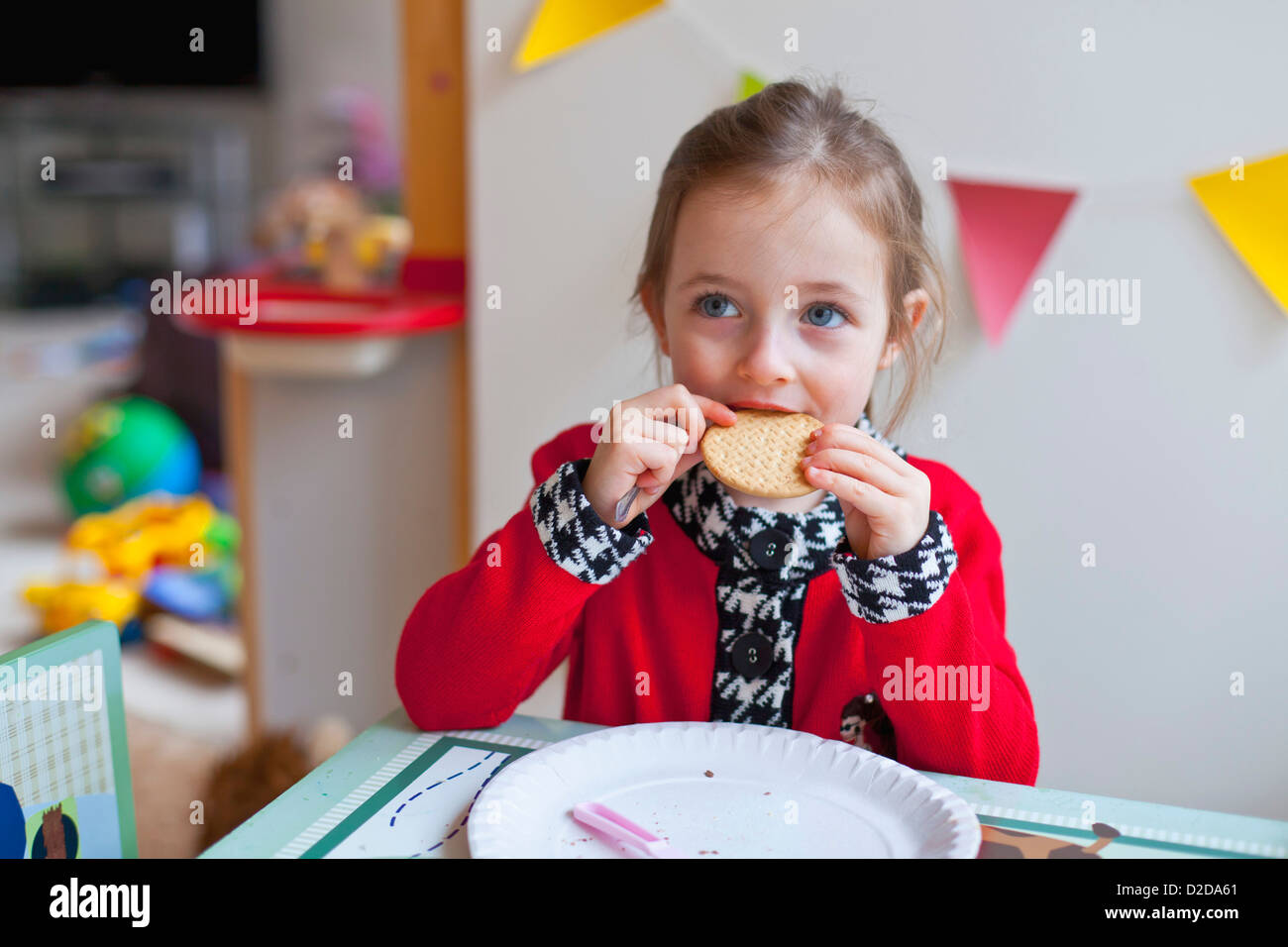 A little girl sitting at a table, taking a bite out of a cookie Stock ...