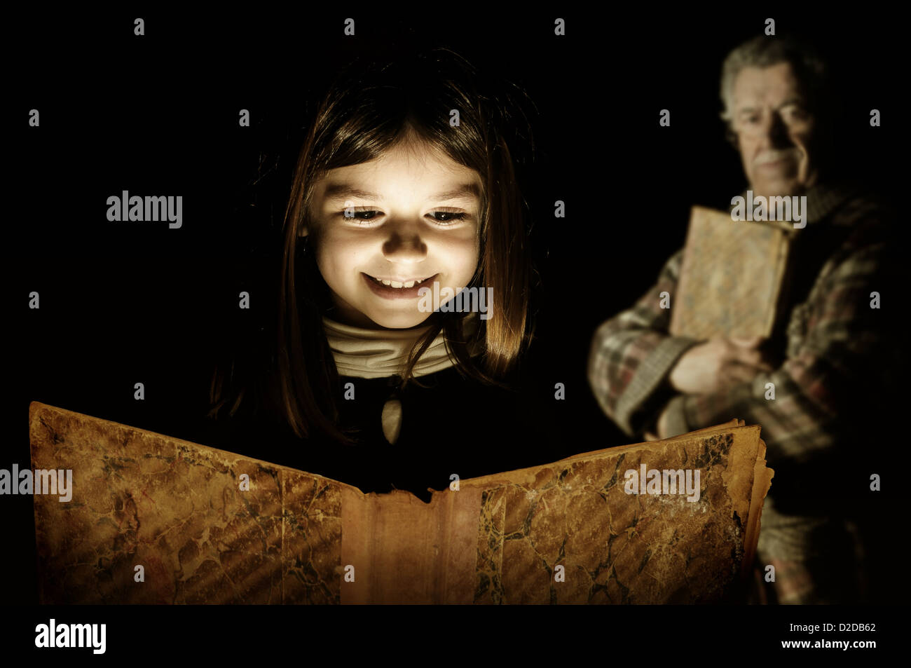 Young girl reading a very old book with grandfather in the background ...